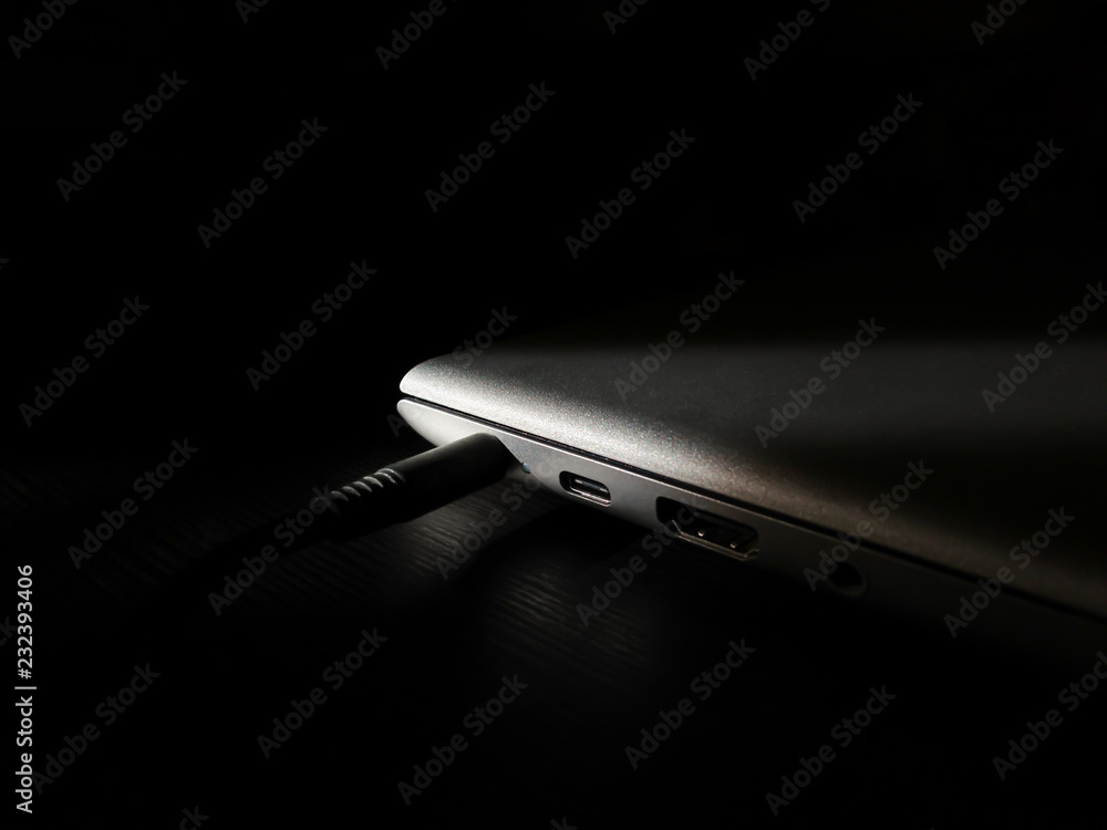 The hi-tech notebook is connected to the adapter charging port in black ...
