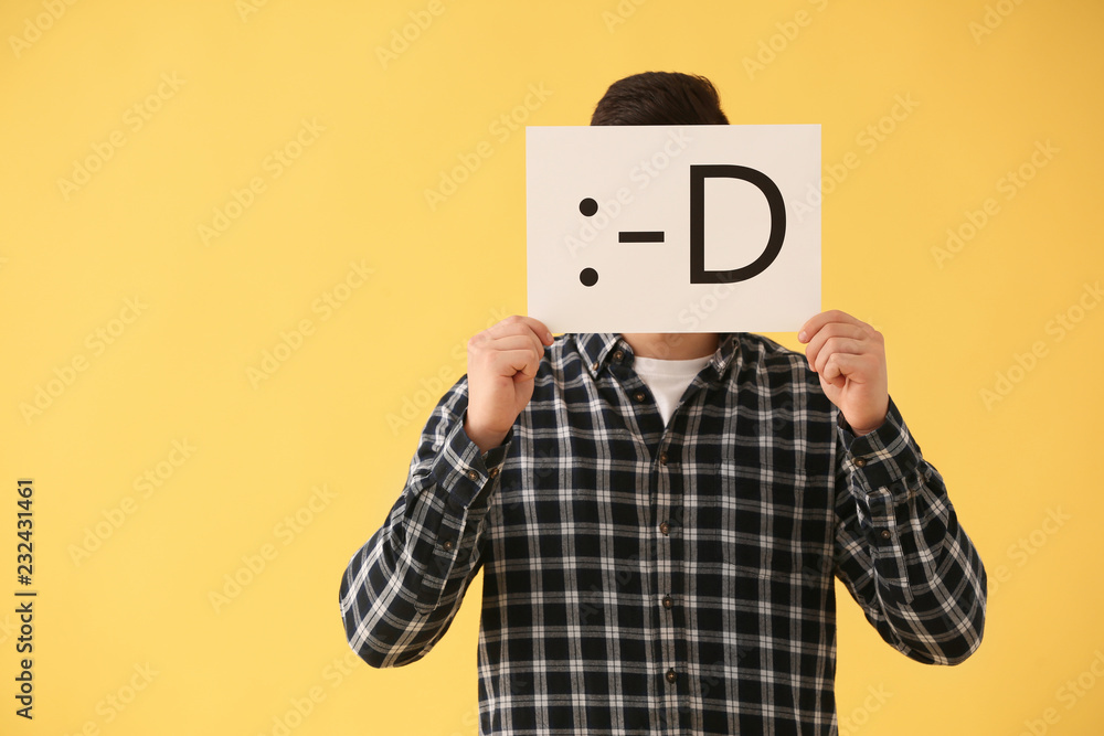 Man hiding face behind sheet of paper with drawn emoticon on color ...