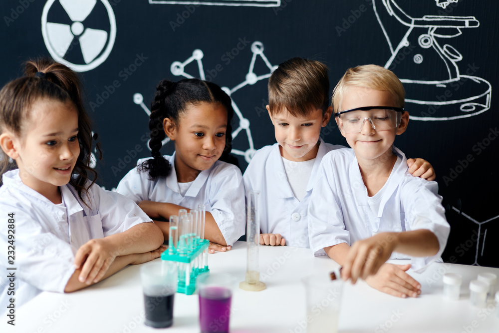 Multiethnic group of 7 years old kids in white lab coats doing a ...