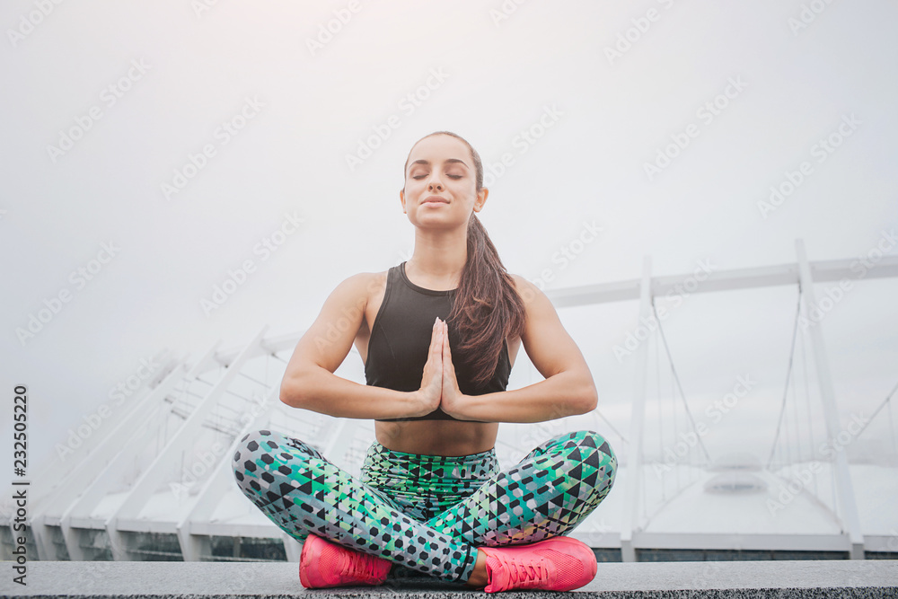 Foto de Young woman sits in lotus position and kees hands together. She ...