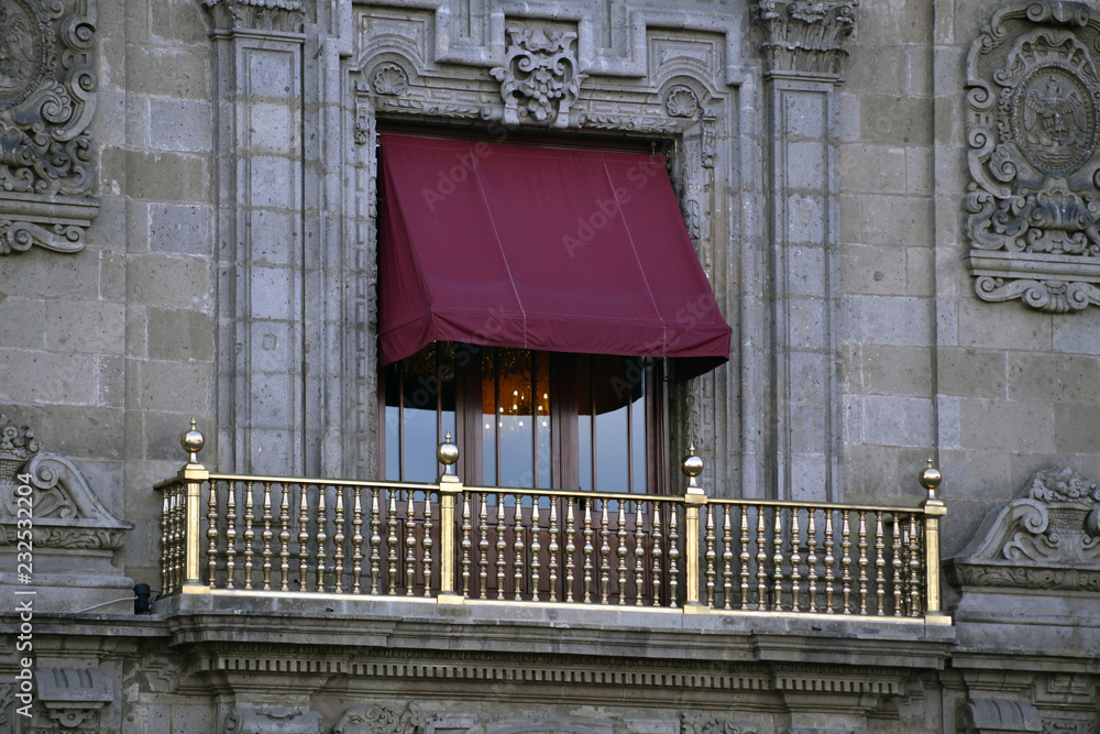 A golden balcony and a window with a red awning above. A historical ...