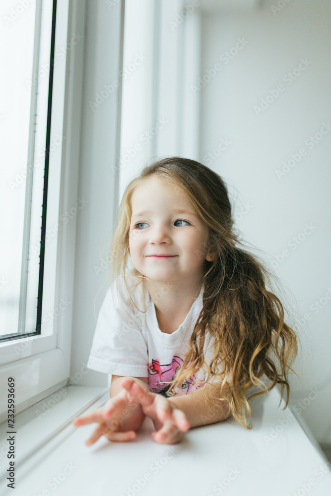 Beautiful little girl smiling and watching out the window. A child ...