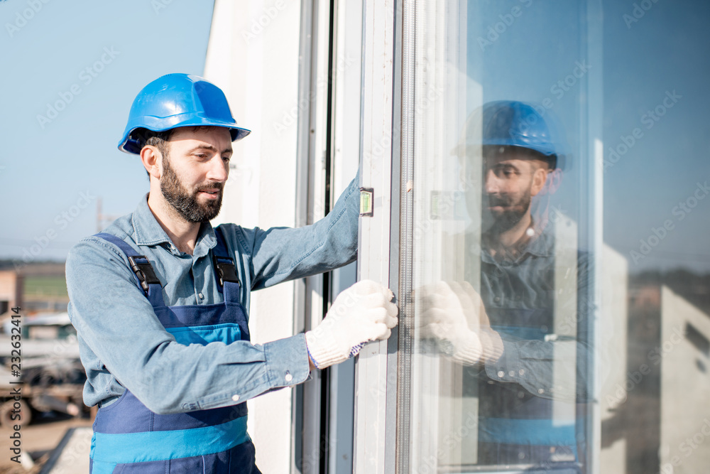 Workman in uniform mounting windows checking the level on the white ...