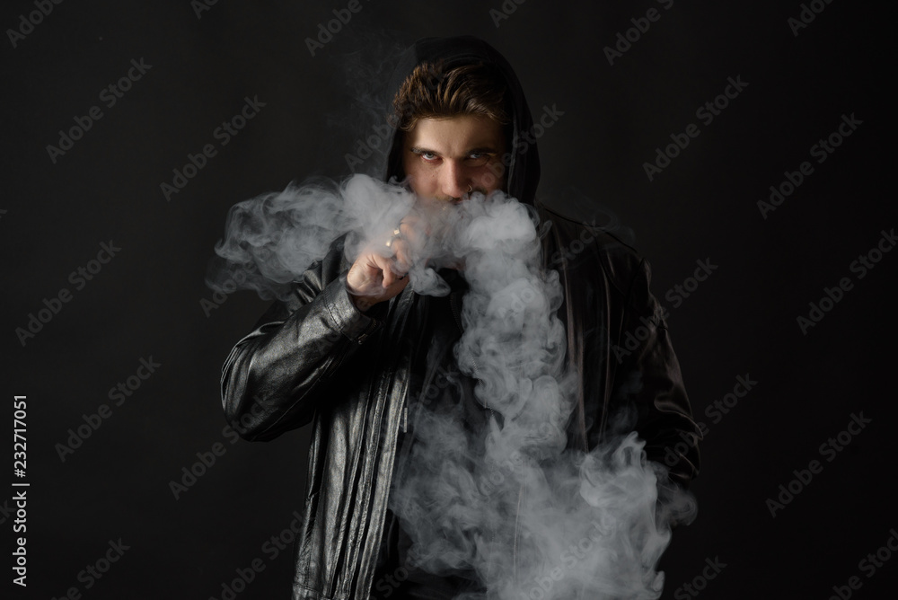 Man with vaping mod exhaling steam at black studio background. Bearded ...