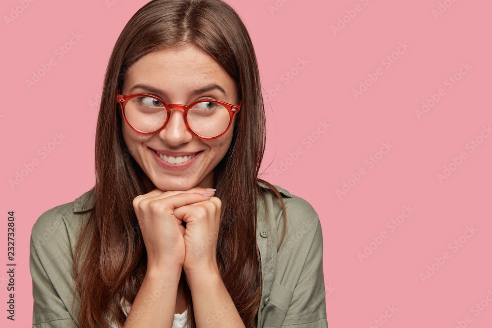 Headshot of dreamy pleased woman with tender smile, wears red rim ...