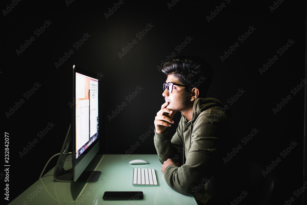 Concentrated asian indian young man in glasses looking at blank screen ...