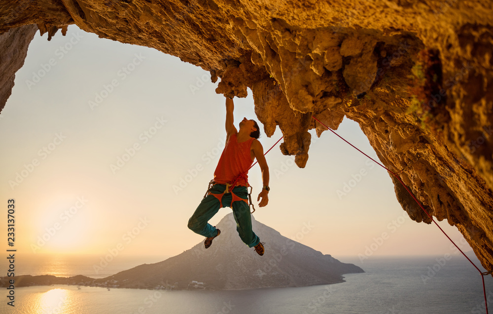Male rock climber hanging with one hand on challenging route on cliff ...
