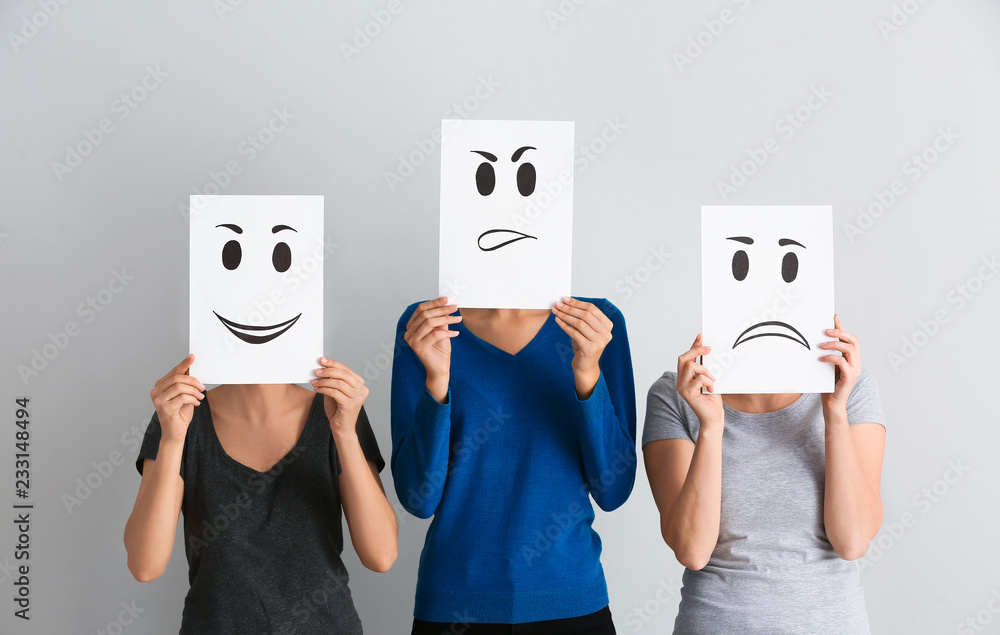 Young women hiding faces behind sheets of paper with drawn emoticons on ...
