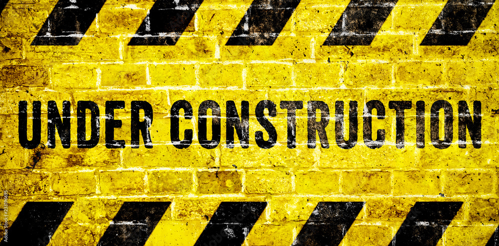 Under construction warning sign with yellow and black stripes on brick ...
