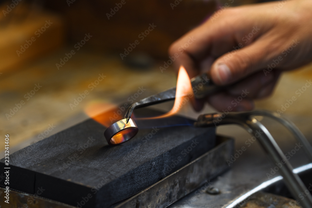 goldsmith hand is glowing a golden wedding ring with a gas flame, copy ...