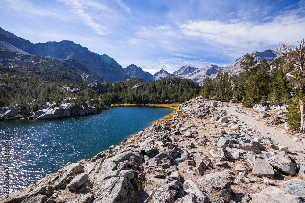 Hiking trail following the shoreline of an alpine lake surrounded by ...