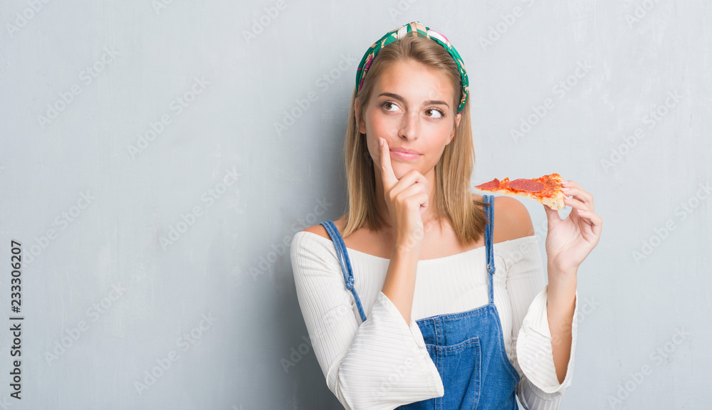 Beautiful young woman over grunge grey wall eating pepperoni pizza ...