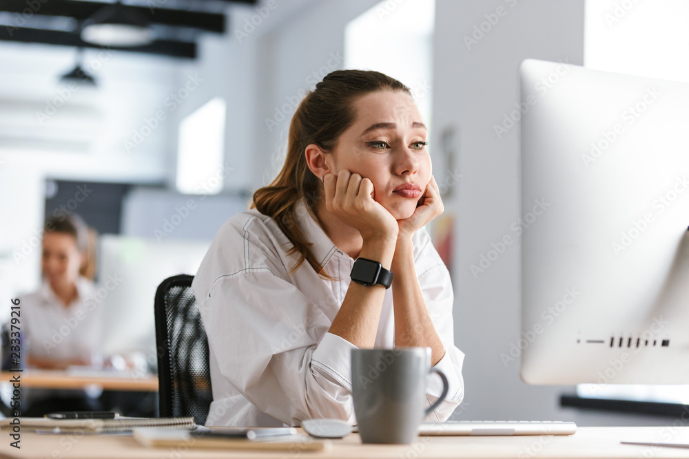 Bored young woman dressed in shirt sitting at her workplace foto de ...