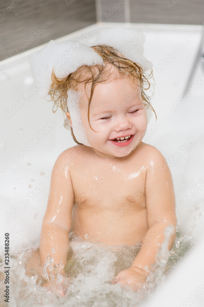 Happy little cute girl bathes in a bath with foam and soap bubbles and ...