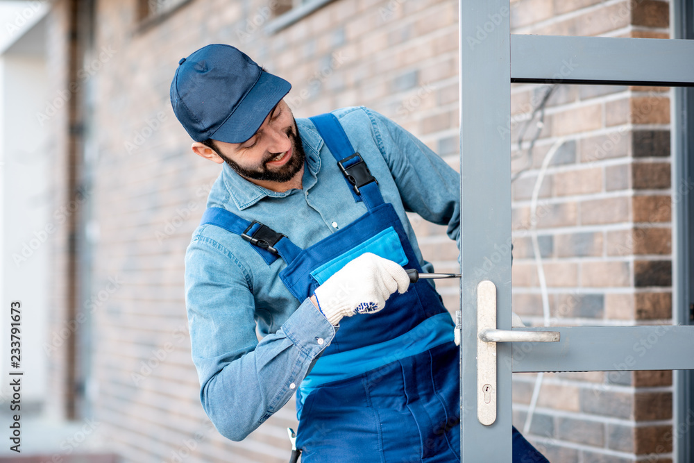 Builder in uniform installing a door lock into the entrance door of a ...