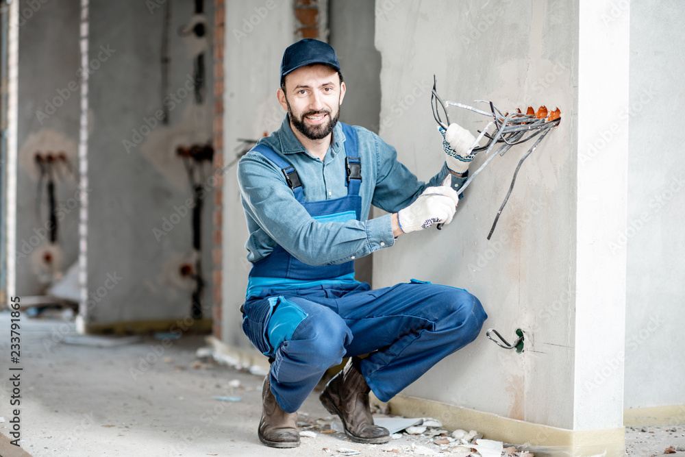 Portrait of an electrician mounting wiring for electric sockets on the ...