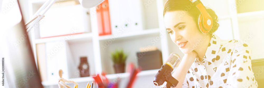 Beautiful young girl sitting in headphones and with microphone at table ...