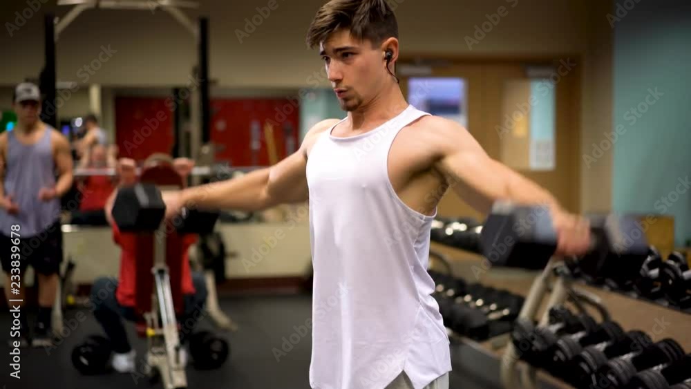 Side shot of young bodybuilder doing dumbbell shoulder fly or lateral ...