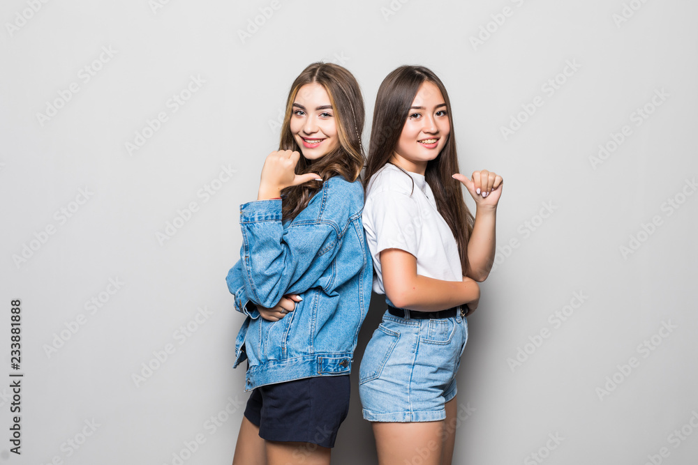 Two pensive young girls dressed in summer clothes standing back to back ...