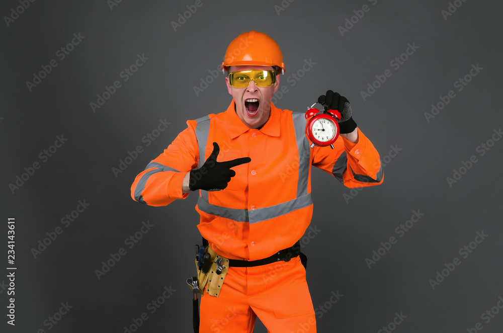Angry builder foreman in the hardhat is showing a red alarm clock in ...