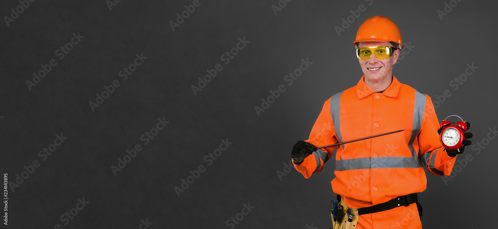 Happy builder worker is showing on a red alarm clock in his hand ...
