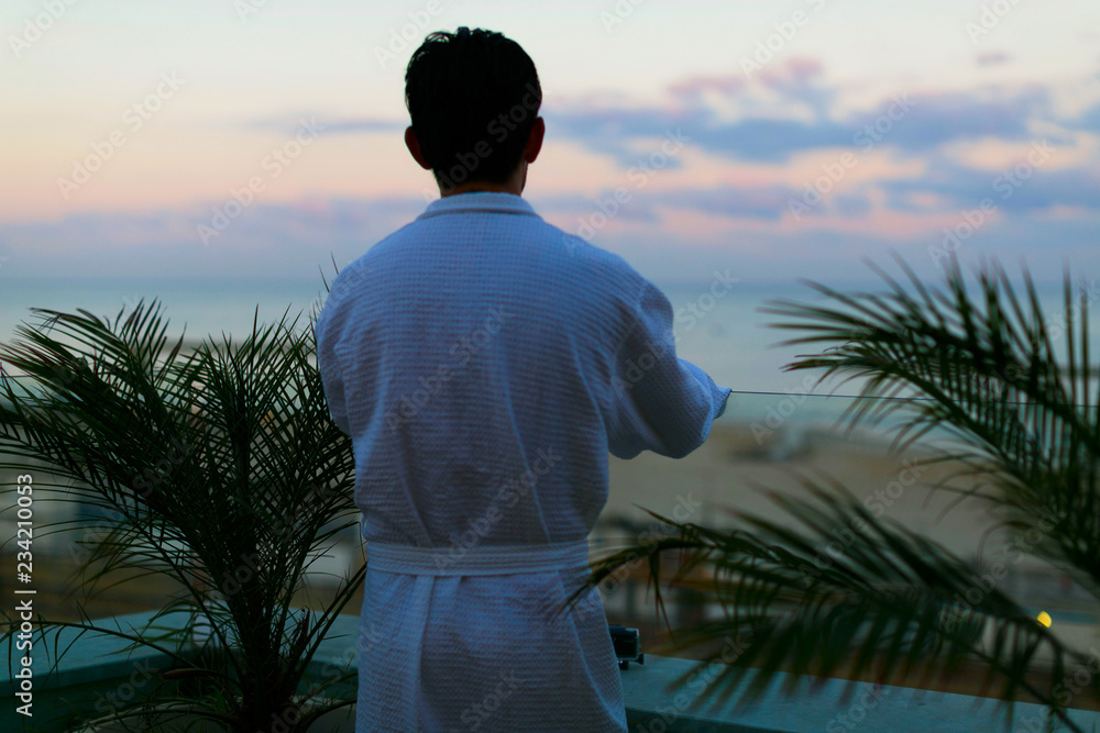 beautiful sunset on the beach. guy in a hotel bathrobe enjoying the sea ...