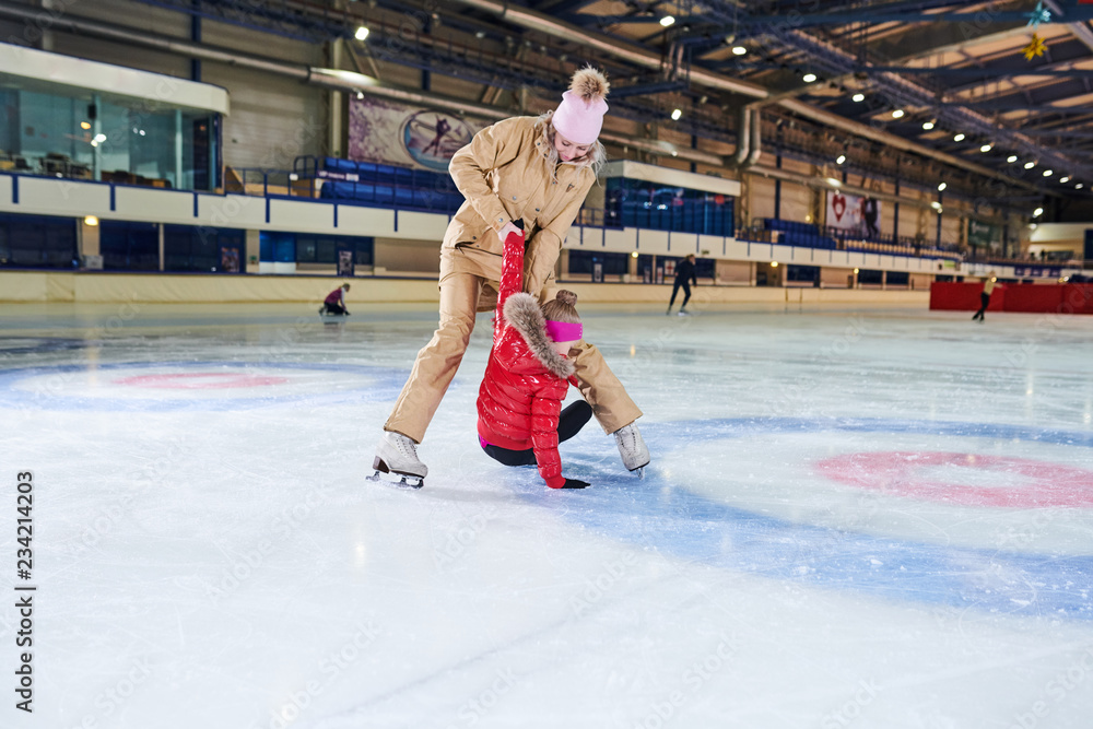 Full length portrait of little girl falling on ice while learning to ...