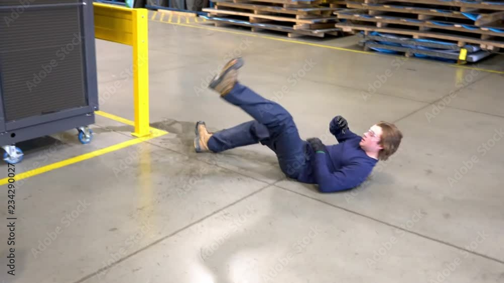 A young male worker slipping on a wet floor in a factory. An industrial ...