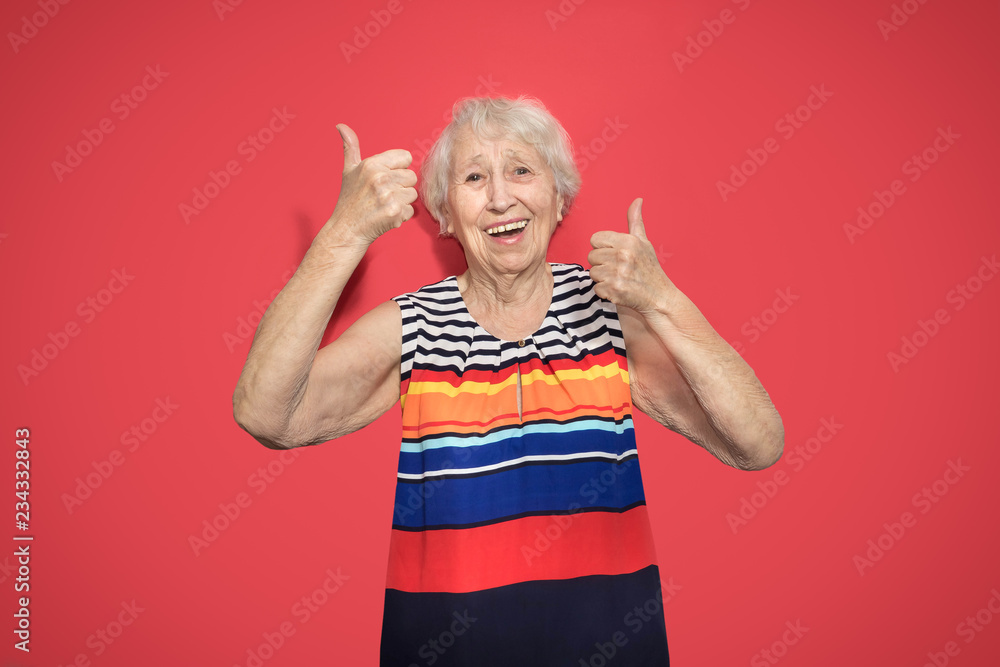 Old smiling woman with surprised expression on her face on red studio ...