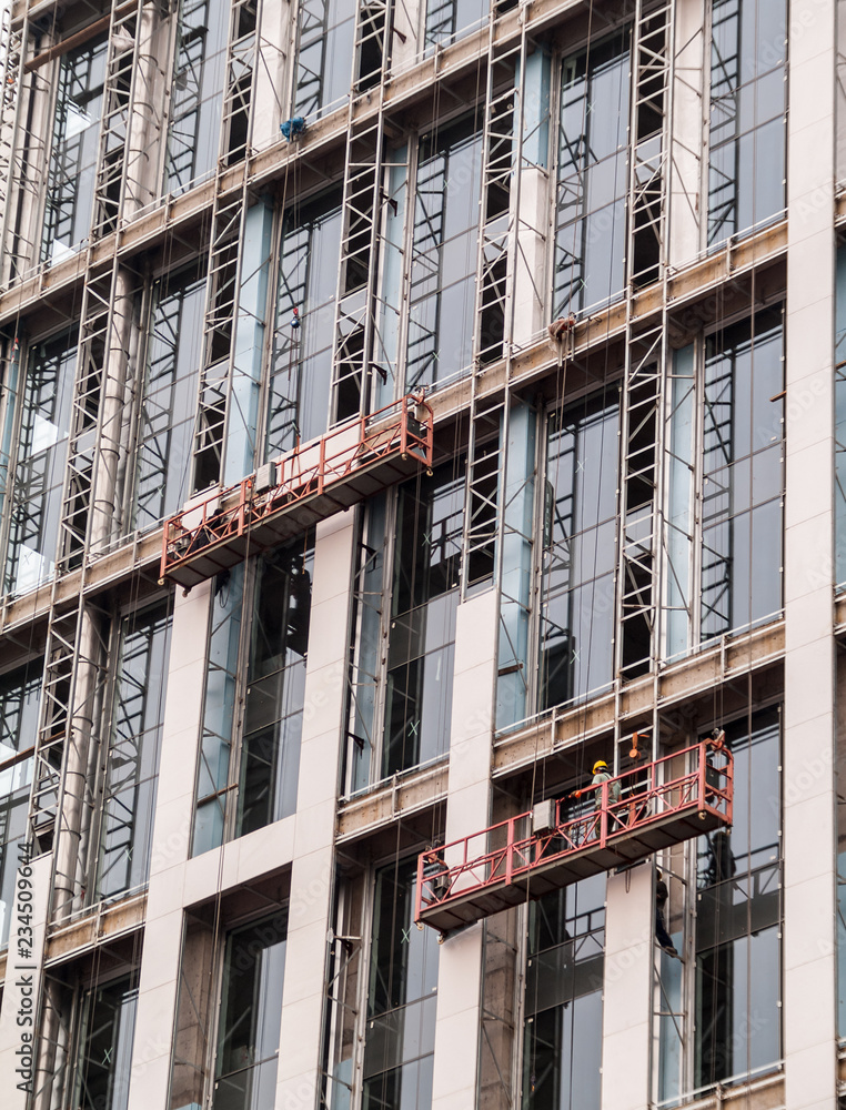 Construction workers on a suspended platform on a skyscraper facade ...