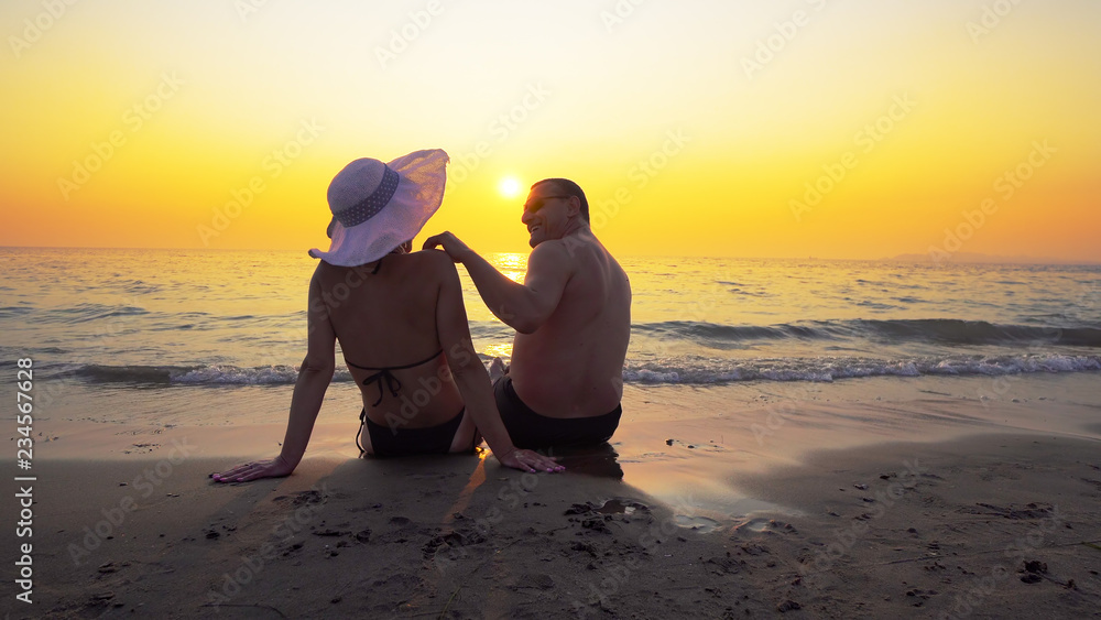 Romantic couple on honeymoon sitting on beach sunset and exchange emotions touching. Summer sea ...