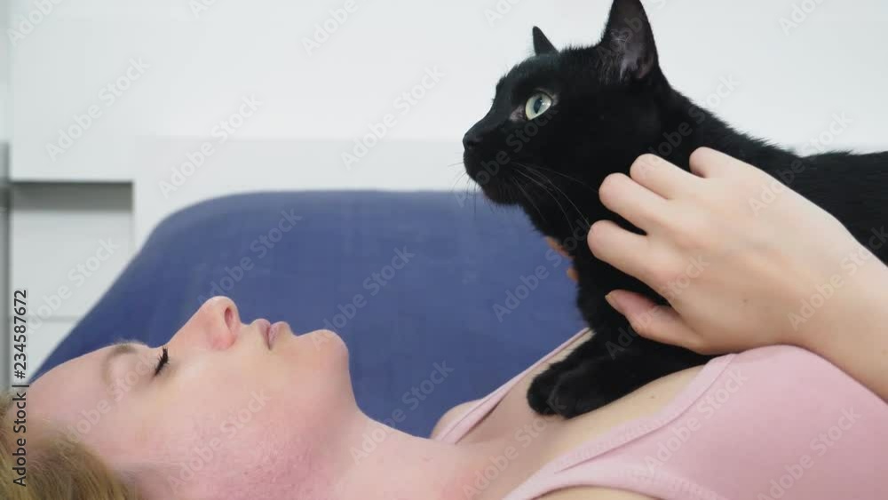 Girl with a cat. Beautiful blonde girl lying in bed and caressing her ...