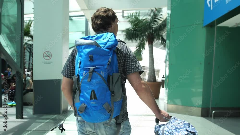 Back of view of young man with backpack pulling suitcase in modern ...