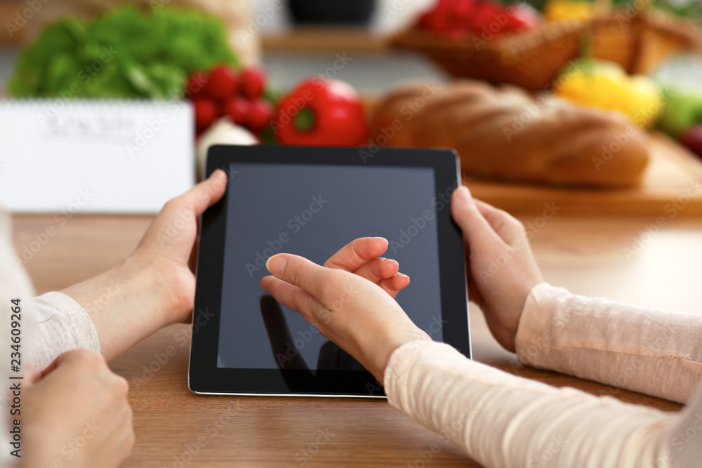 Close-up of human hands using tablet or touch pad. Two women in kitchen ...
