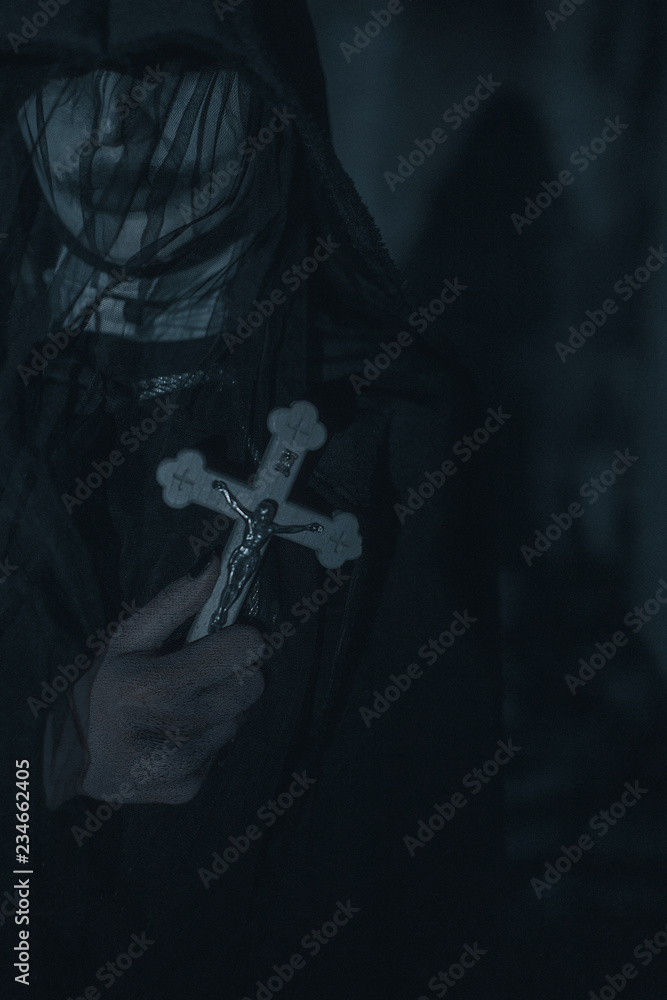 Woman is standing in a darkness with a cross in her hand in an image of ...