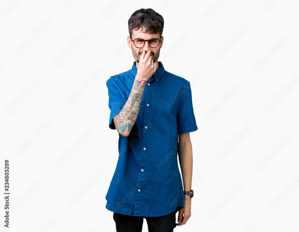 Young handsome man wearing glasses over isolated background smelling ...