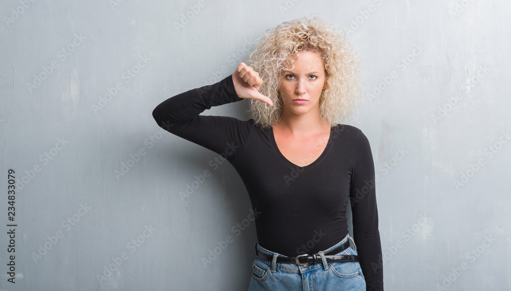 Young blonde woman with curly hair over grunge grey background with ...