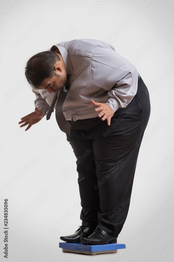 Obese man in formal clothes standing on a weighing machine bending ...