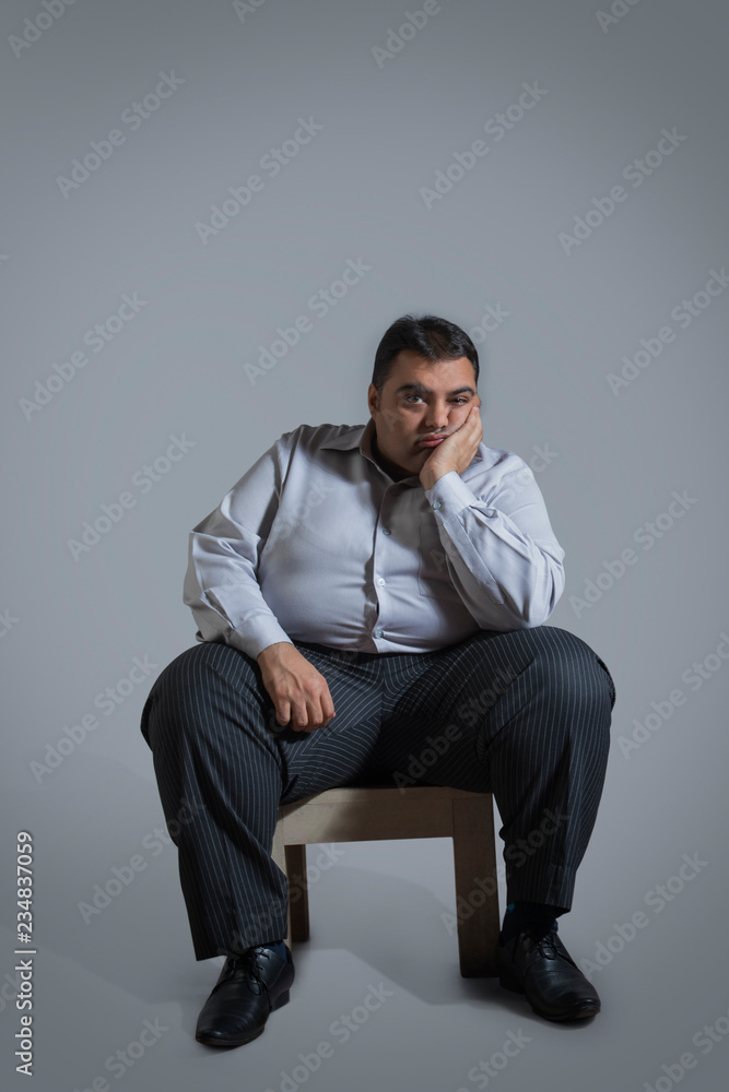 Overweight man sitting on chair in sad mood with chin resting on hand ...