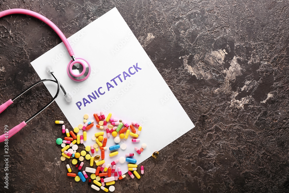 Paper with text PANIC ATTACK, stethoscope and scattered pills on grey ...