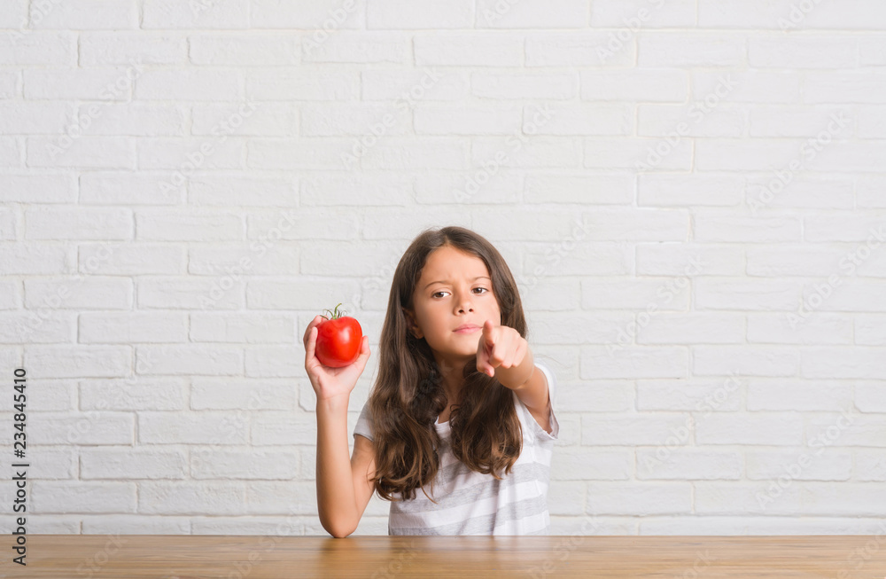 Young hispanic kid sitting on the table eating fresh tomato pointing ...