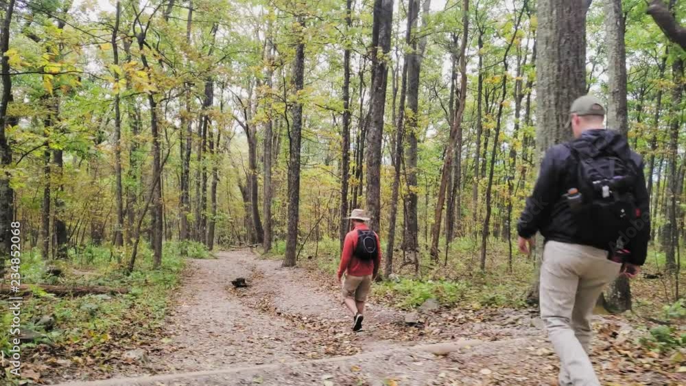 Two men hike along a trail through the mountains taking in the autumn ...