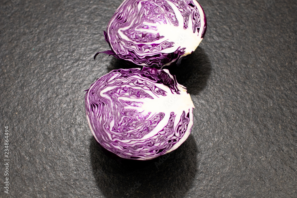 red cabbage ball cut in half with all the leaves on a black granite ...