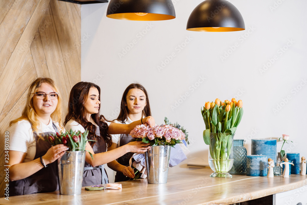 Team of three females florists working while standing behind wooden ...