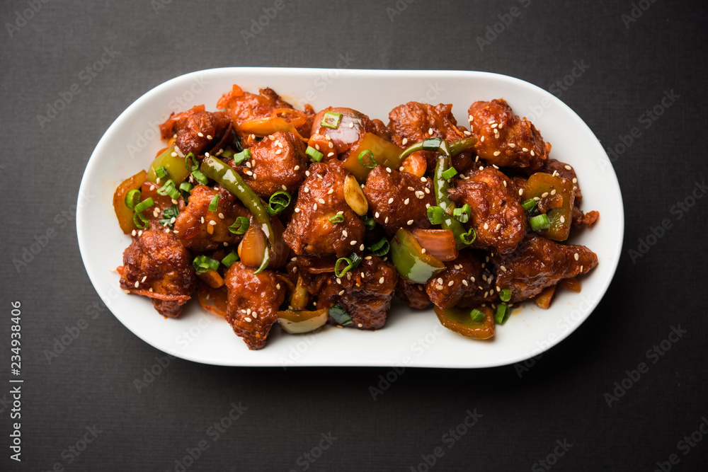 Indian Chilli Chicken dry, served in a plate over moody background ...