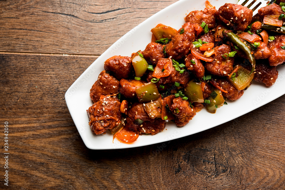 Indian Chilli Chicken dry, served in a plate over moody background ...