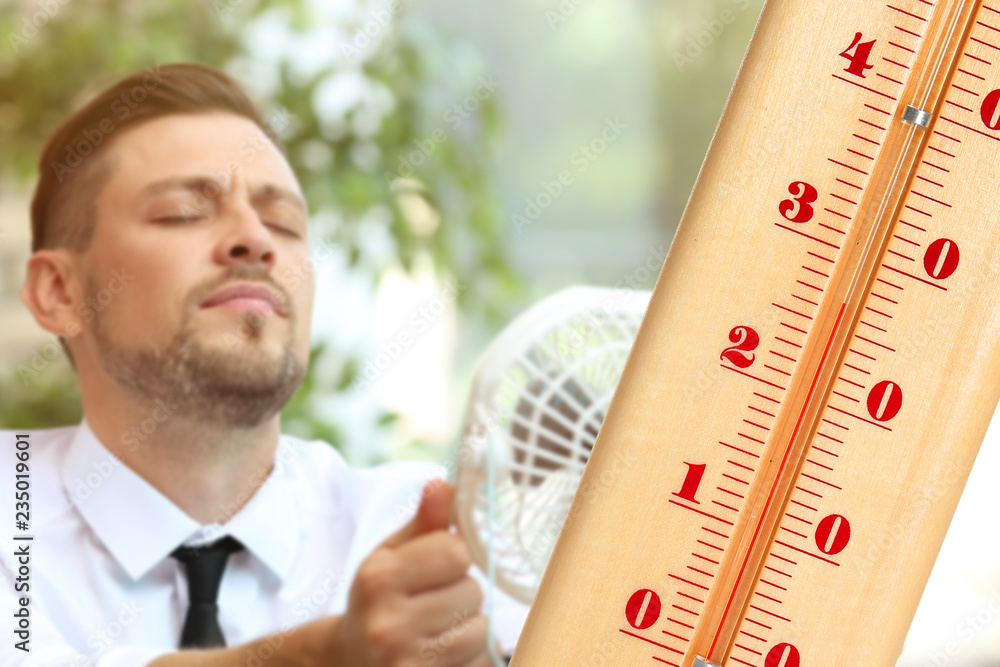 High temperature on thermometer and man suffering from heat in office ...