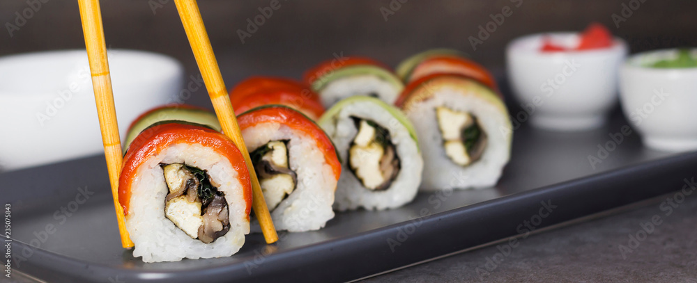 Sushi rolls on grey plate picked by bamboo chopsticks, wasabi, ginger ...