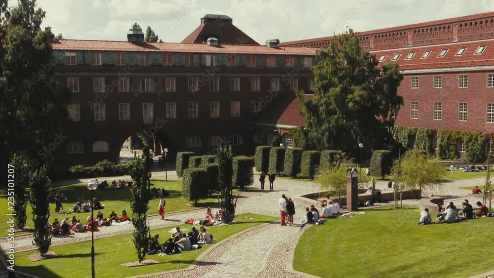 Wide view of students relaxing on the lawn of a courtyard on their ...