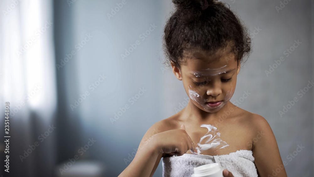 Nice preschool female child putting cream on body and face, copying mom ...